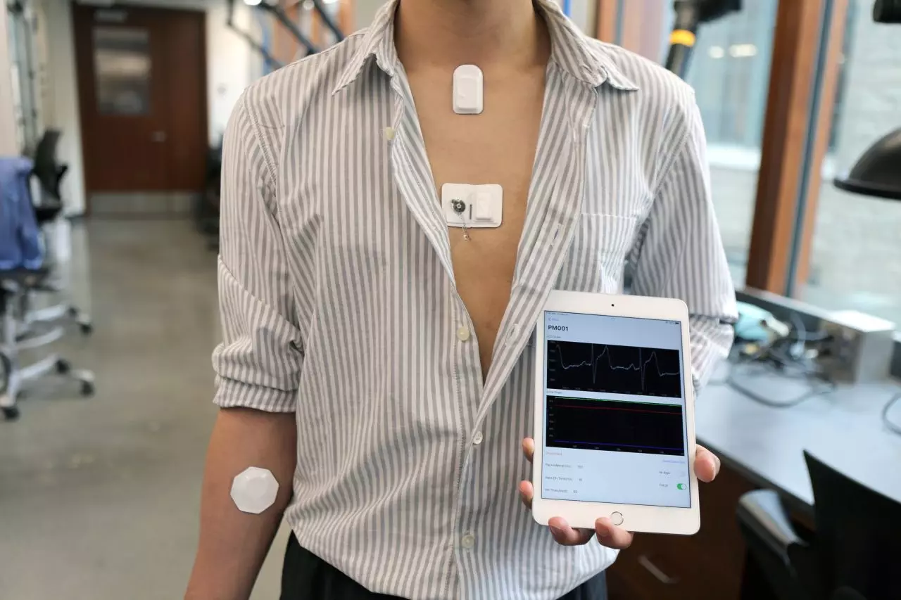 Un volontario che mostra i sensori wireless e l'unità di controllo del sistema aggiornato del pacemaker, che può anche inviare dati a un'app visualizzata sul tablet.