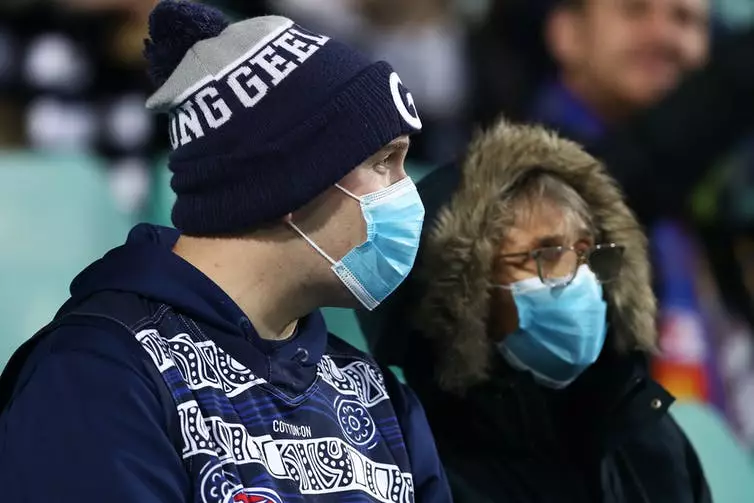 Duas pessoas assistindo a uma partida de esportes usando máscaras