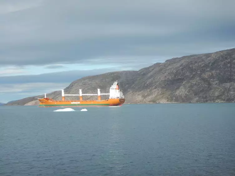 Un barco naranja se encuentra en agua helada con una pendiente rocosa detrás.