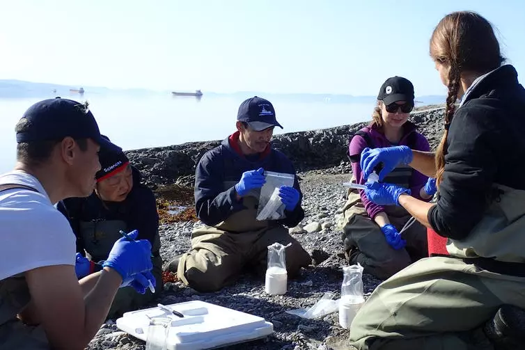 Grupa ludzi siedzi na brzegu i uczy się korzystać ze sprzętu do pobierania próbek.