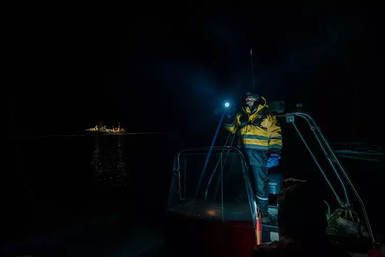 Un hombre en un bote se para con una antorcha, mirando hacia la noche polar.
