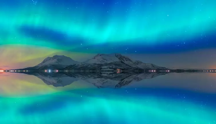 空のターコイズブルーの光の帯が、下のノルウェーのフィヨルドに反射しています。