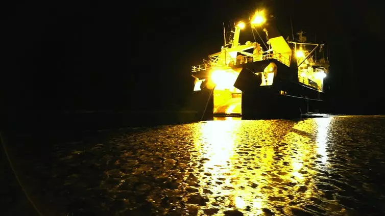 पीली रोशनी में ढका एक बड़ा जहाज बर्फीले पानी को रोशन करता है।