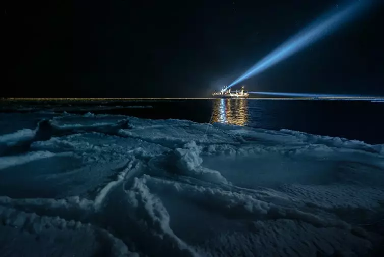 海氷から見ると、地平線上にある大きな船が白い光を空に向けています。