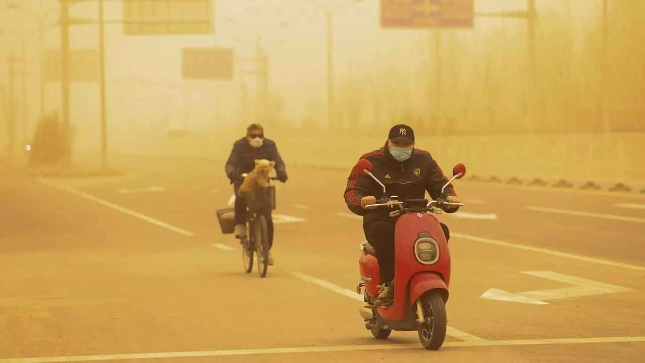Mensen die beschermende maskers dragen fietsen door een straat tijdens een zandstorm op 15 maart 2021 in Peking, China. De Chinese hoofdstad en de noordelijke delen van het land werden maandag getroffen door een zandstorm, waardoor luchtkwaliteitsindexen van PM 2,5 en PM 10 naar duizenden werden gestuurd en vluchten werden geannuleerd.