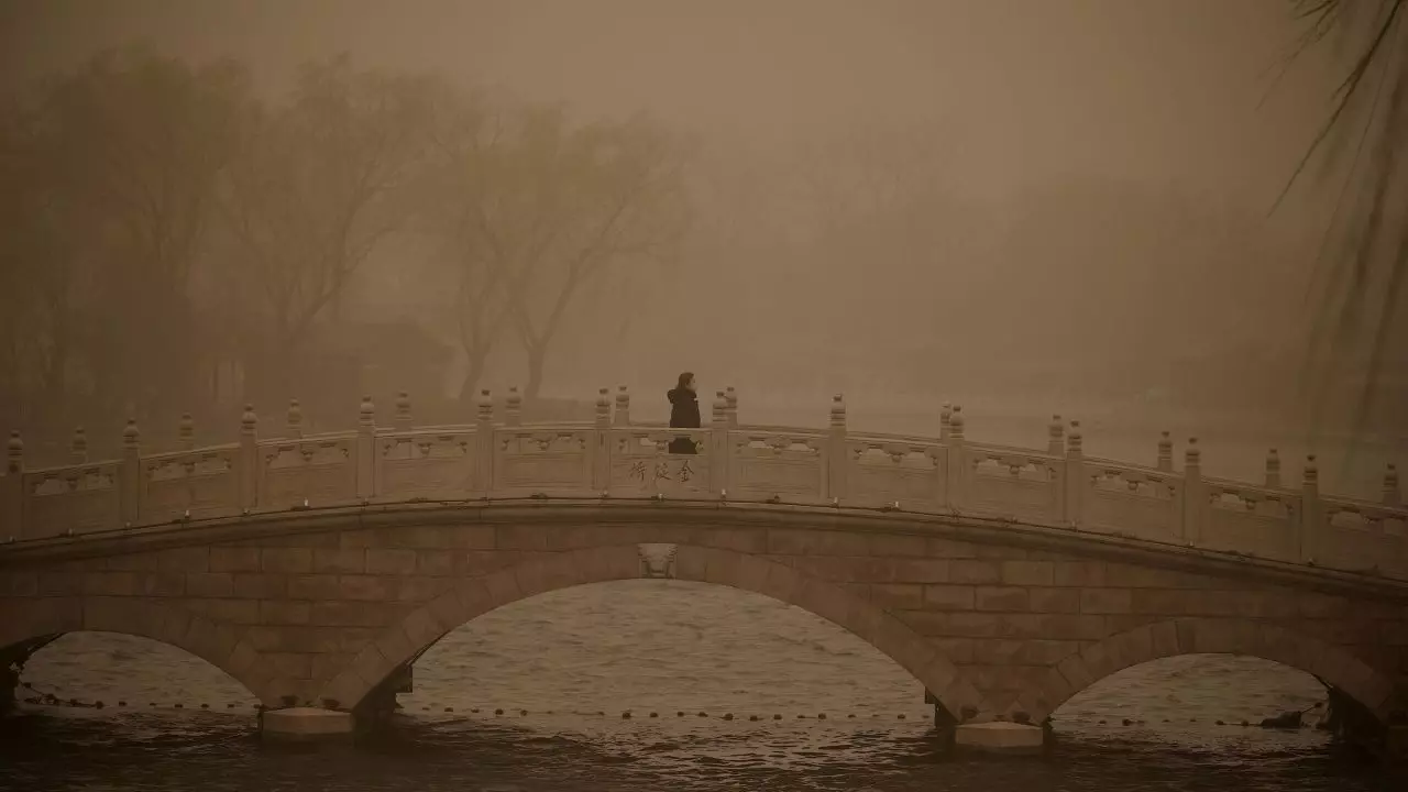 15 मार्च, 2021 को बीजिंग में एक रेतीले तूफान के दौरान एक महिला हुहाई झील पर एक पुल को पार करती है।