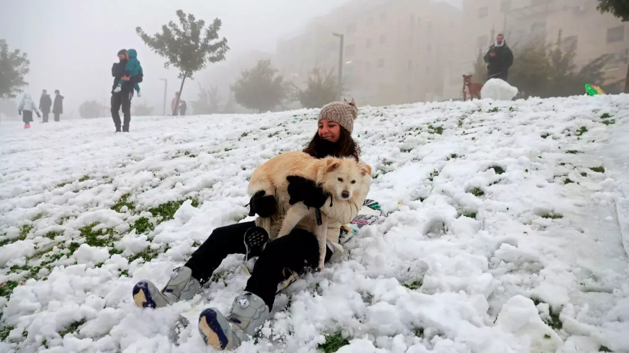 2021년 2월 18일 예루살렘에서 눈보라가 몰아친 후 개를 안고 있는 여성이 눈 덮인 비탈을 미끄러져 내려오고 있습니다.