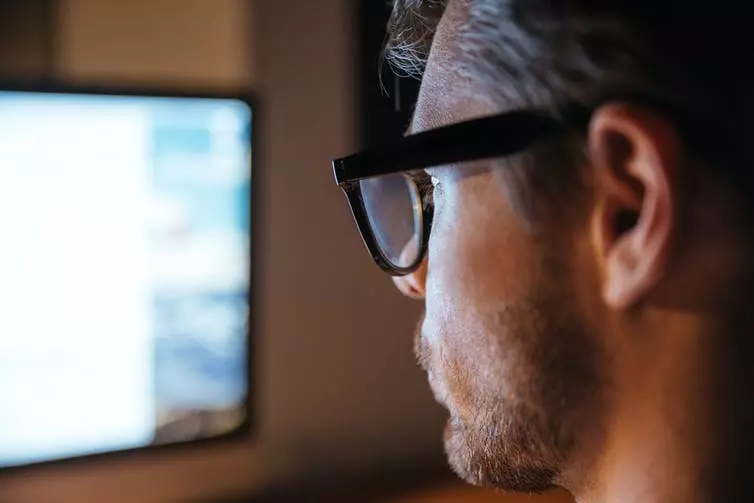 Profil d'un homme regardant un écran d'ordinateur flou.