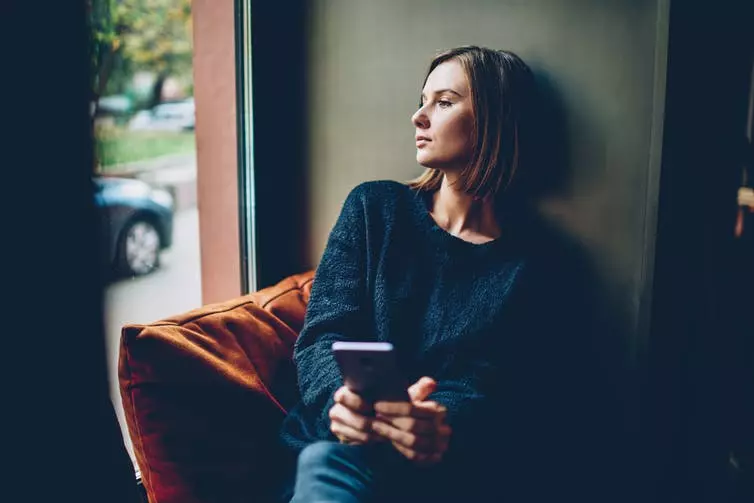 Mujer sosteniendo un teléfono, mirando por la ventana.