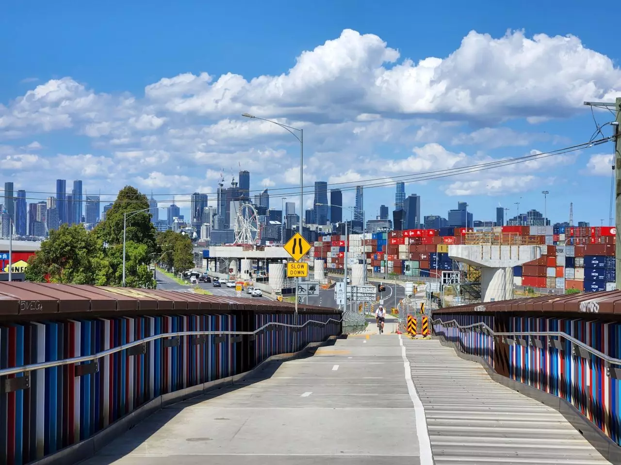 Unha ponte cun ciclista sobre ela, o horizonte da cidade de Melbourne ao fondo.